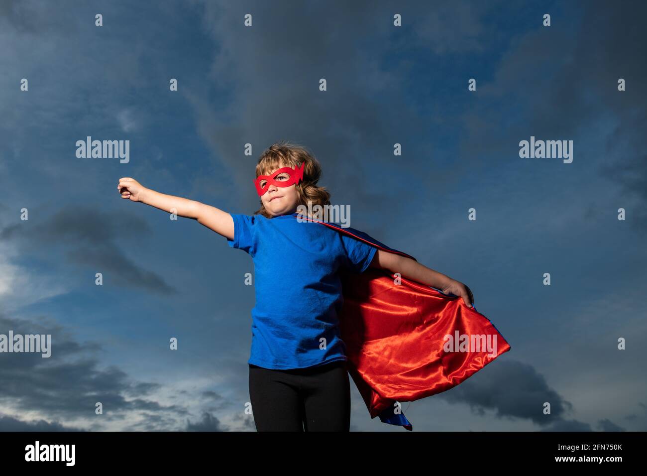 Superhero kid against dramatic blue sky background. Strong super hero ...