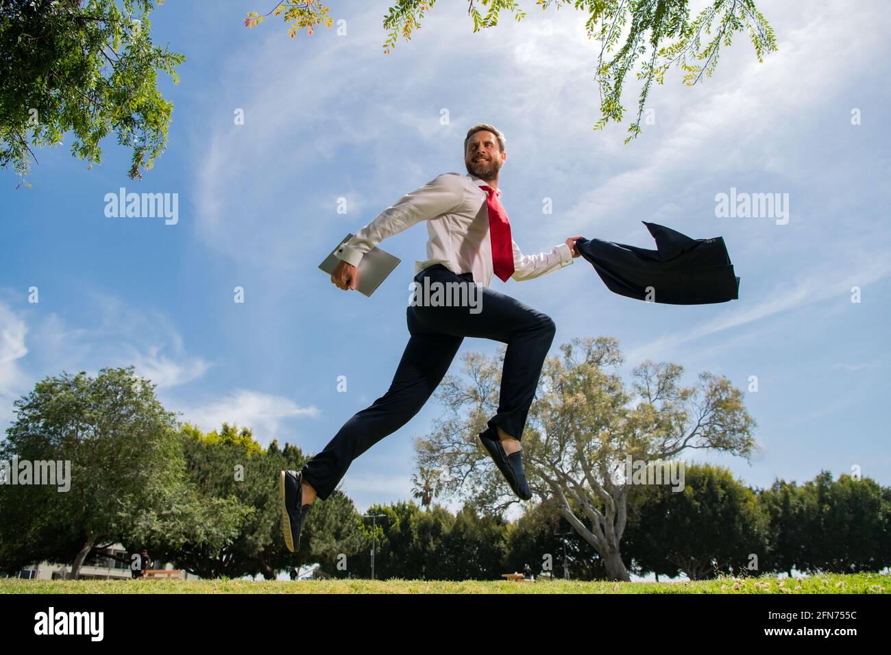Business man in suit jumping over urban park. Portrait of successful ...