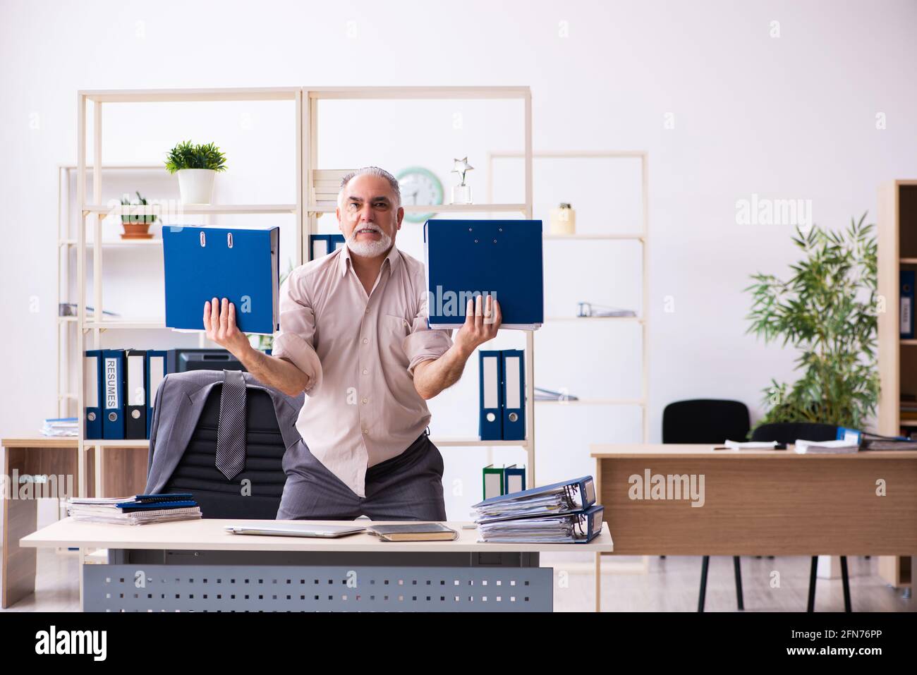 Senior male employee doing physical exercises at workplace Stock Photo ...