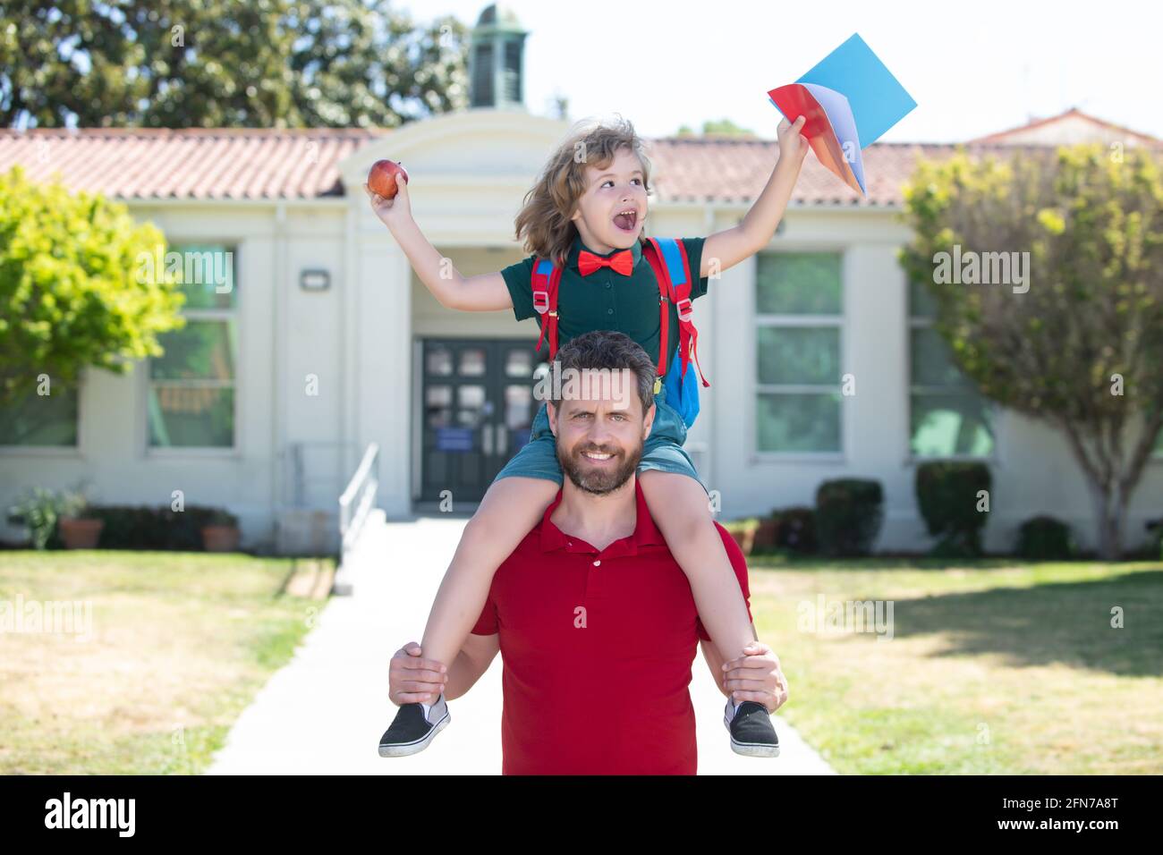 Man and happy amazed child piggyback near school. Father walking son to ...