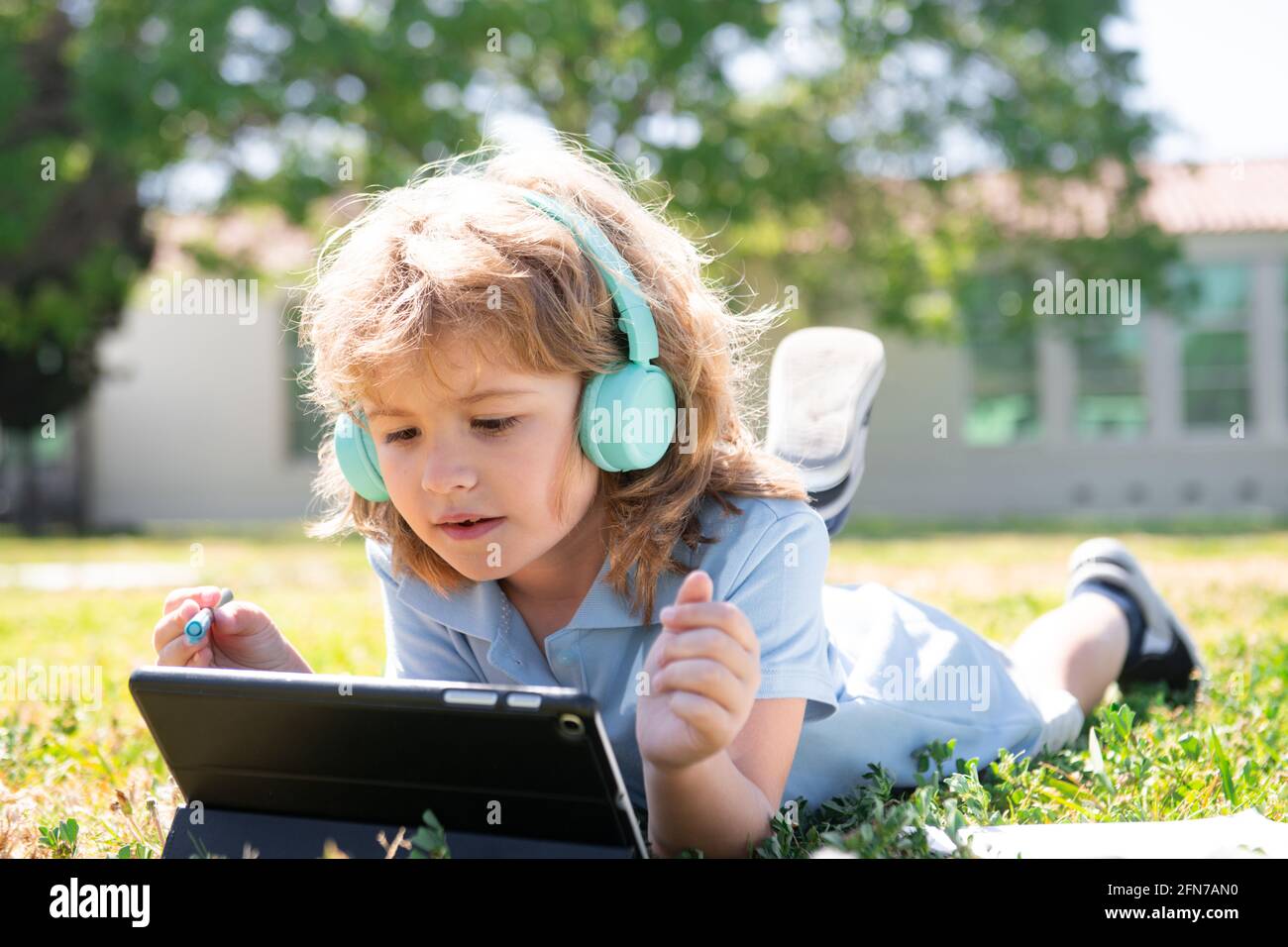 Little schoolboy pupil use notebook or tablet in the park on grass ...