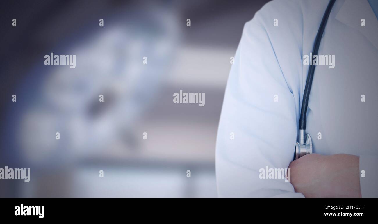 Mid section of male doctor with arms crossed against surgical light in ...