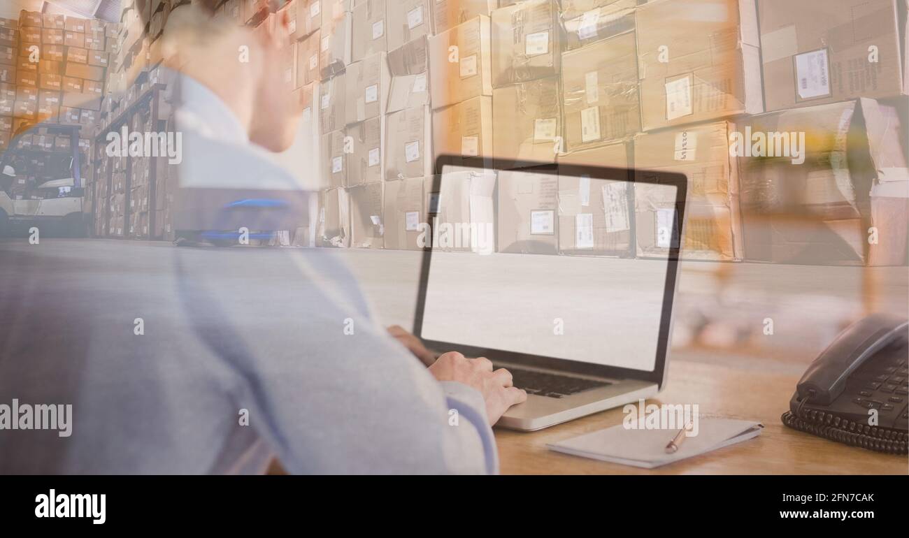 Composition of man using laptop over stacked up boxes in warehouse ...