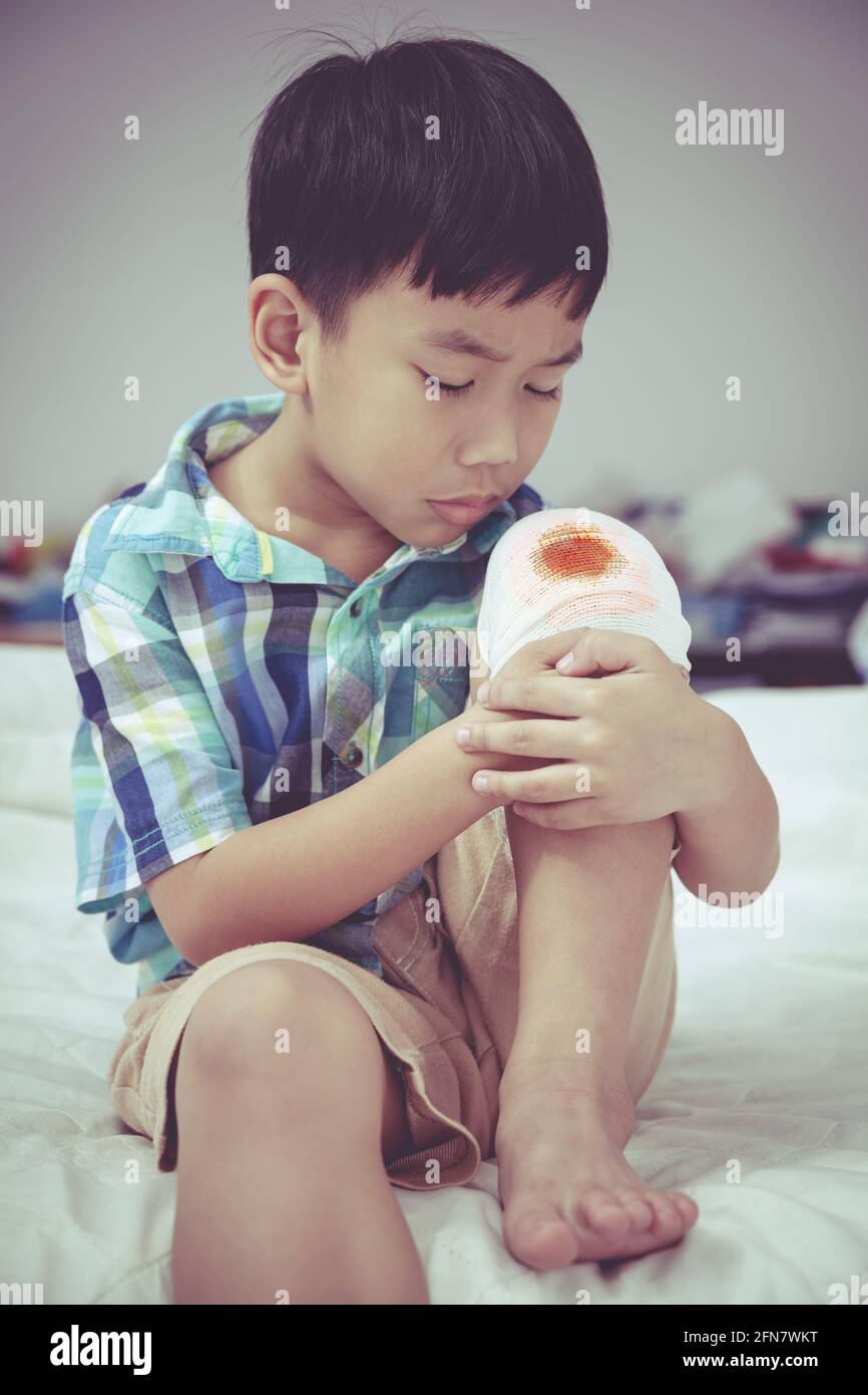 Child injured. Asian handsome boy looking at wound on his knee with ...