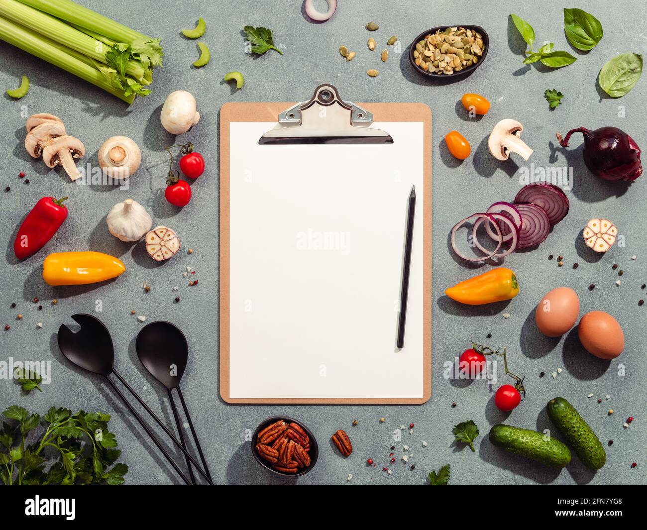 Food ingredients, salad serving utensils and clipboard with white paper ...