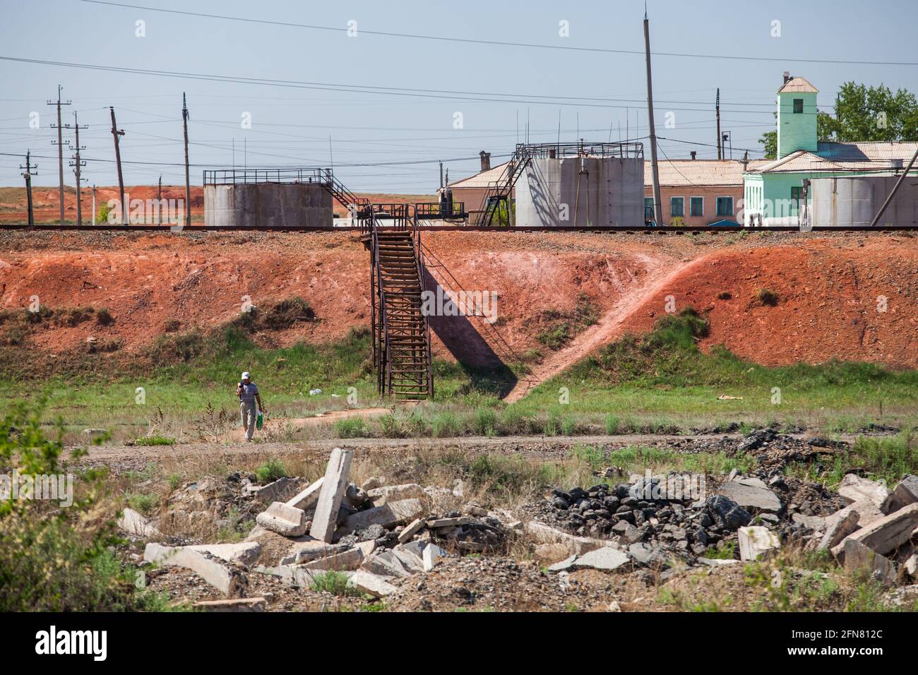 Man crossing field near railway station. Red bauxite clay ground ...