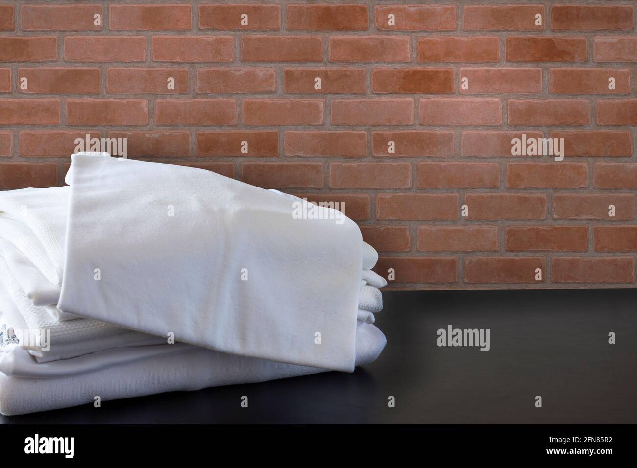 Pile of white clothes in front of red brick wall and on black floor ...