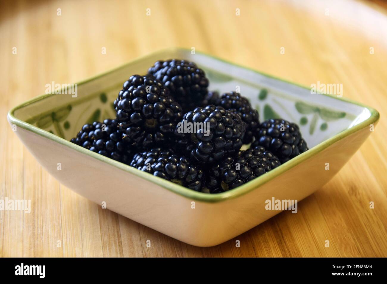 Large ripe blackberries are in decorative square ceramic bowl on bamboo ...
