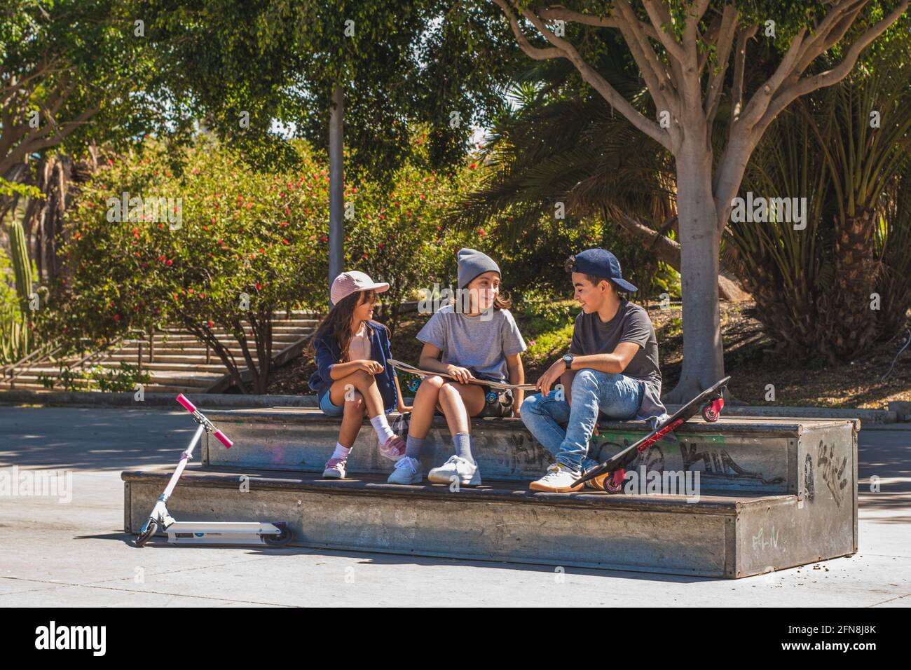 Three Caucasian children, sitting with their skates in an obstacle of a ...