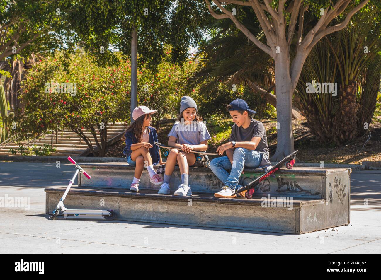Three Caucasian children, sitting with their skates in an obstacle of a ...