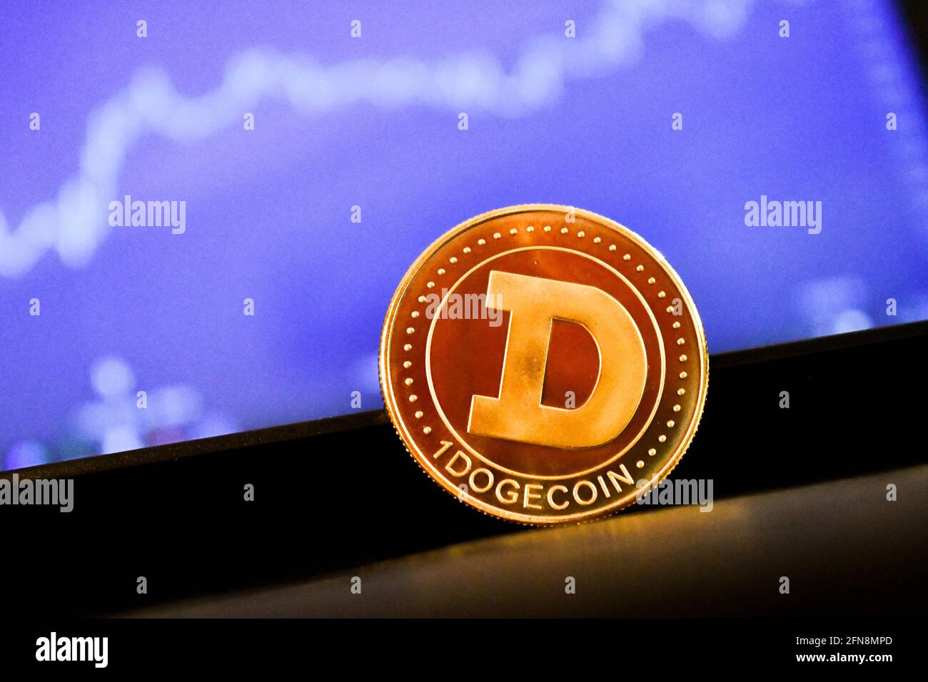 horizontal photograph of a dogecoin token in front of a computer screen ...