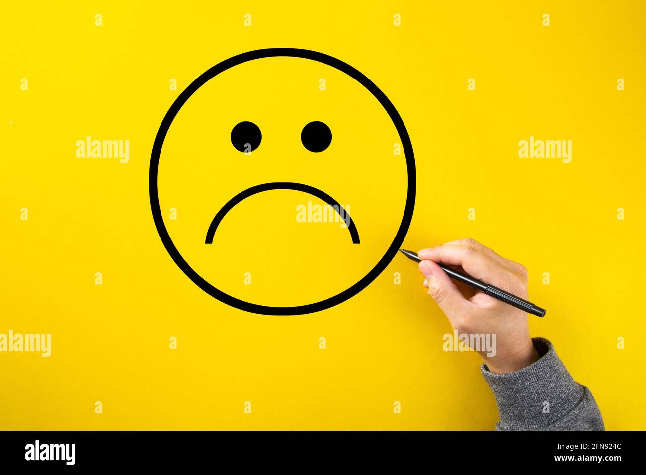 Male hand drawing a sad face sketch on yellow background. Client ...