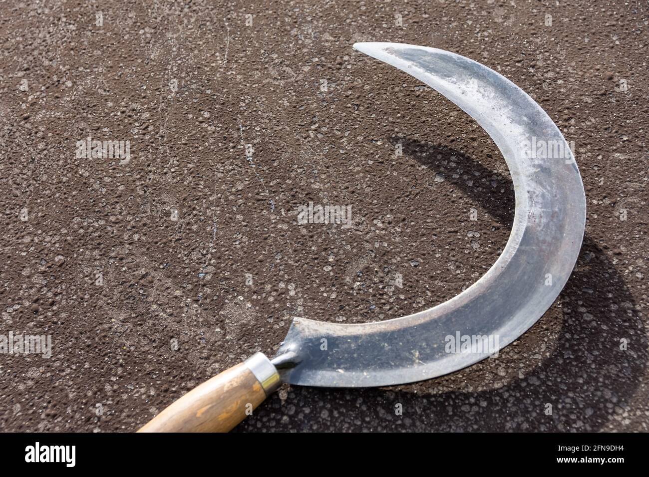Closeup of a dangerously sharp sickle on the ground with its shadow ...