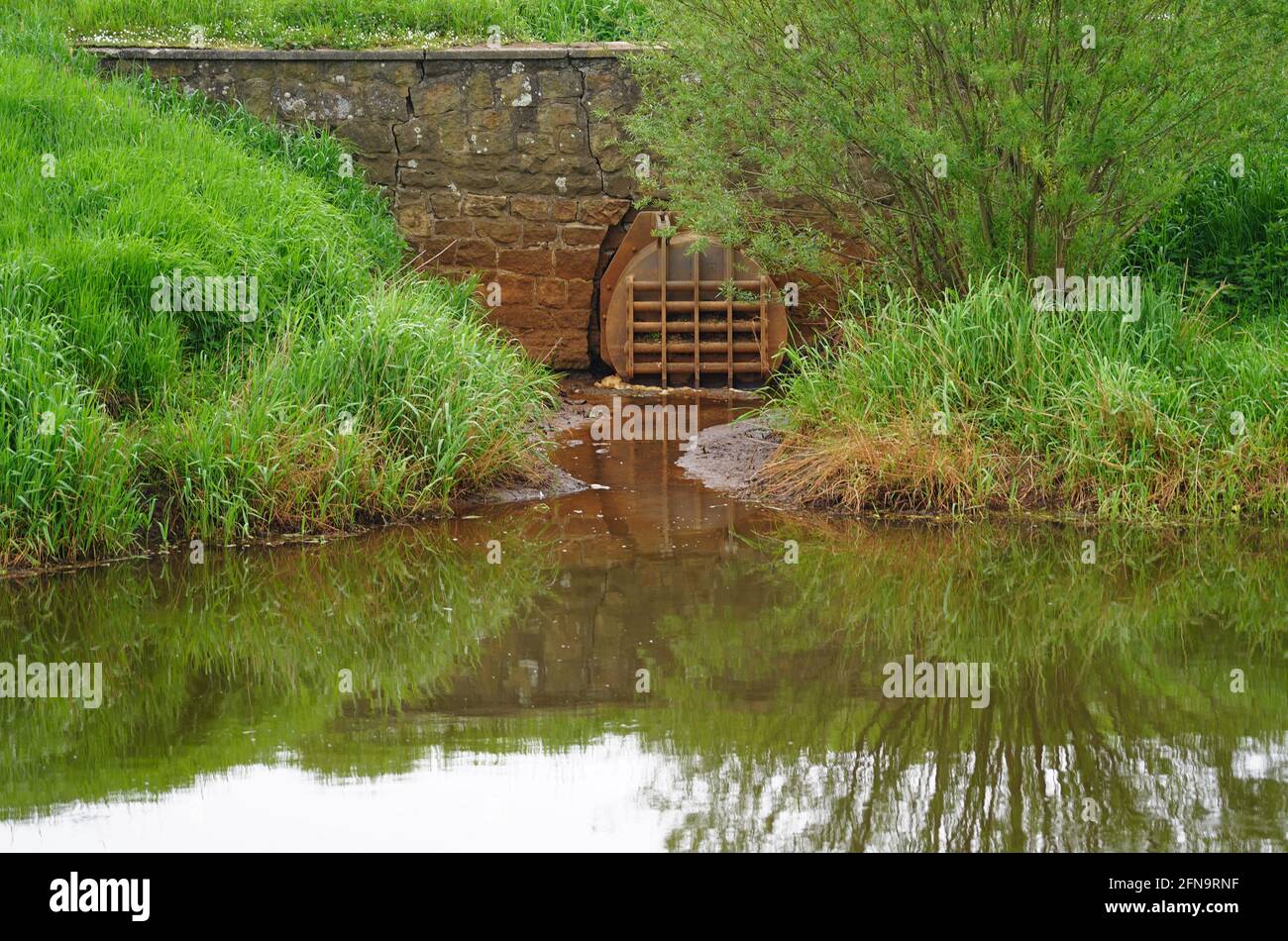 Connection of a stream to the river with a grid. An old wall with a ...