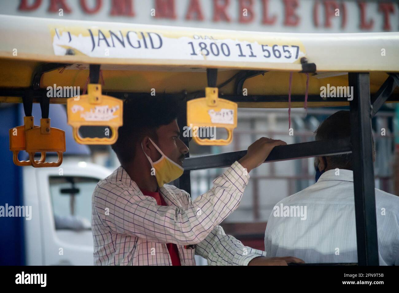 Man in public transport electric auto rickshaw sitting with mask pulled ...