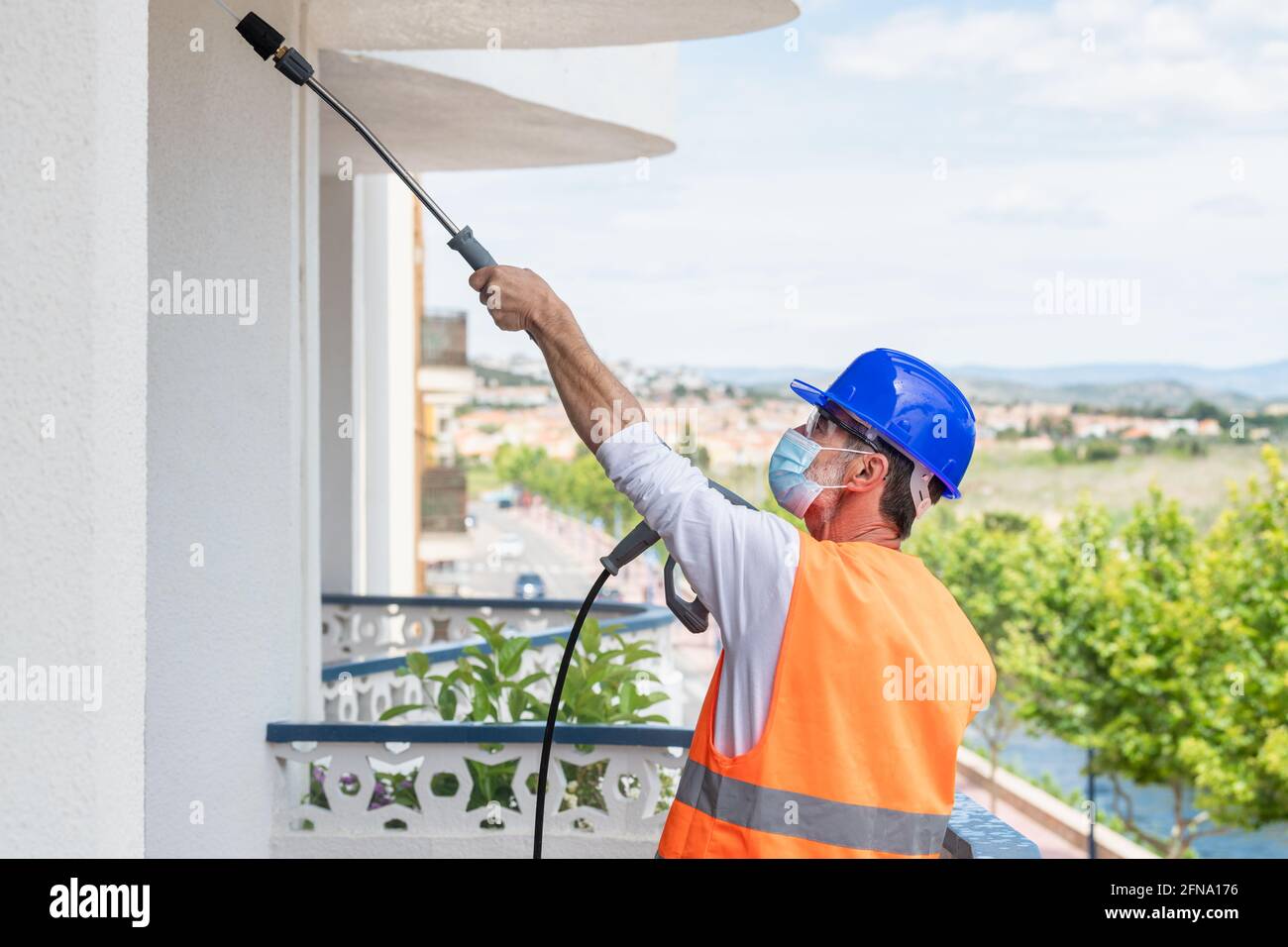 Worker with protective gear cleaning a wall with a pressure washer ...