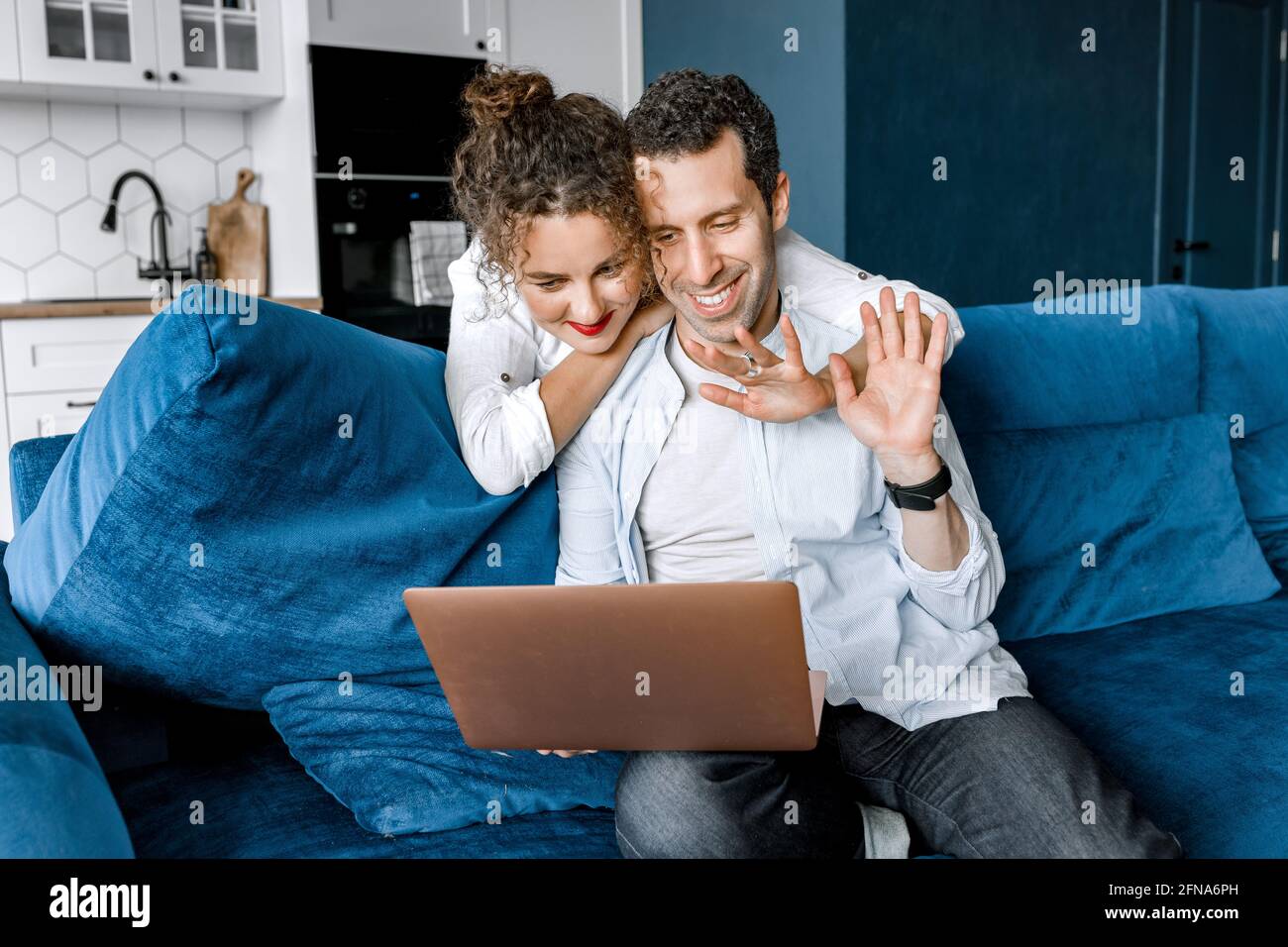 Beautiful young couple cuddle, sit on blue sofa, make video call to ...