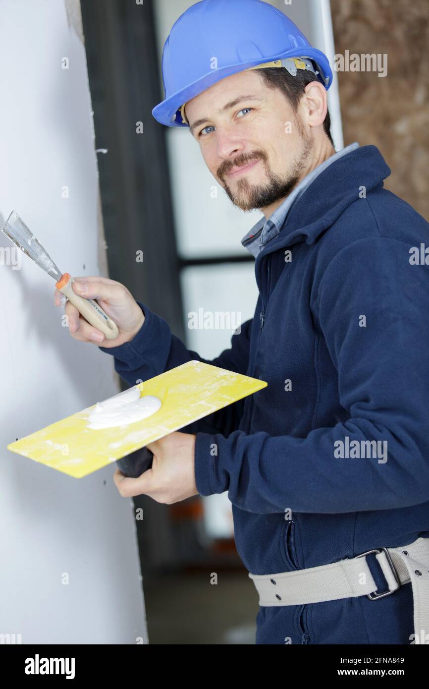 handsome builder in blue working uniform plastering the wall Stock ...