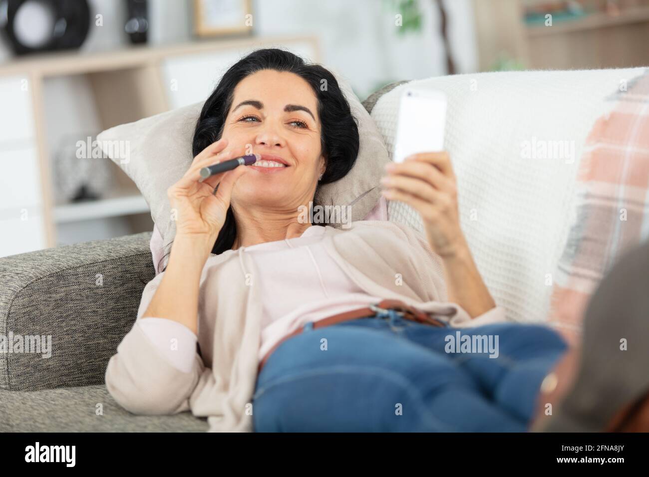mature woman smoking e-cigarette at home laying on sofa Stock Photo - Alamy