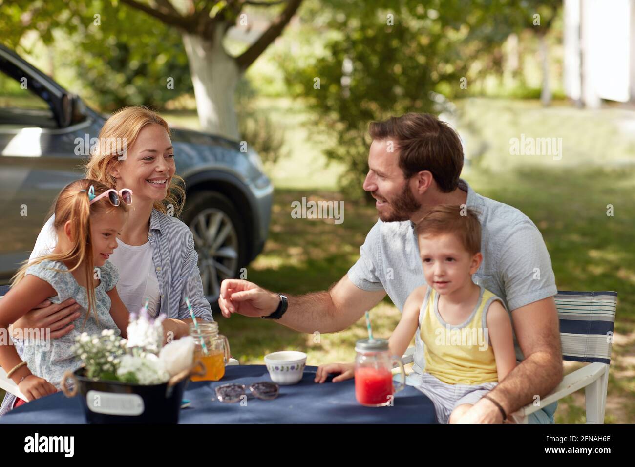 cheerful caucasian family of four talking and sitting at table outdoor ...