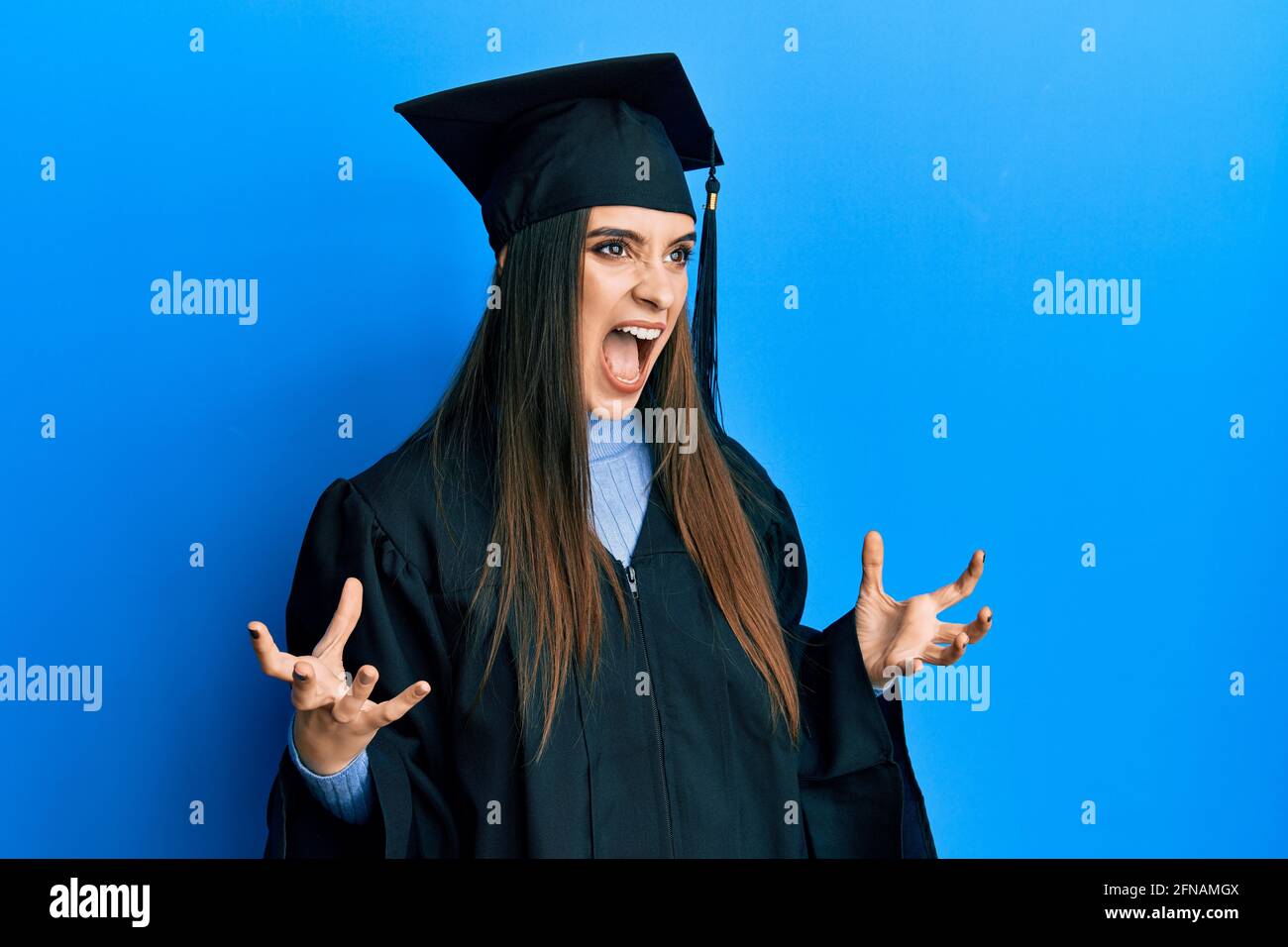 Beautiful brunette young woman wearing graduation cap and ceremony robe ...