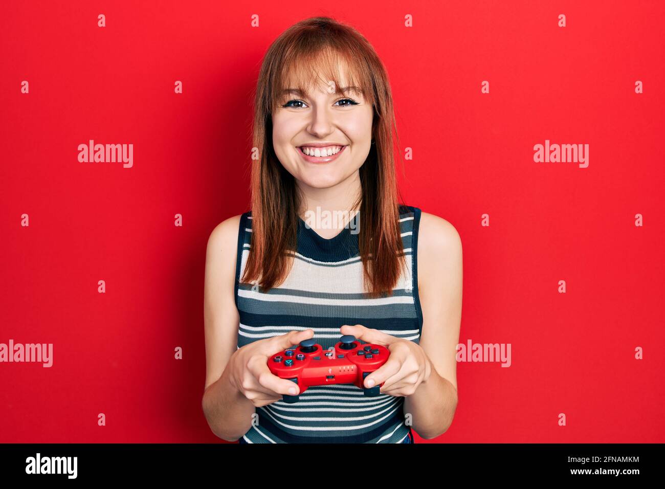 Redhead young woman playing video game holding controller smiling with ...