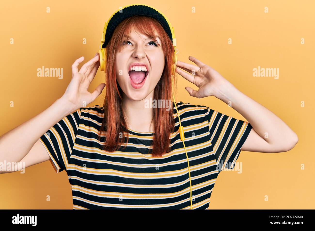 Redhead young woman listening to music using headphones angry and mad ...