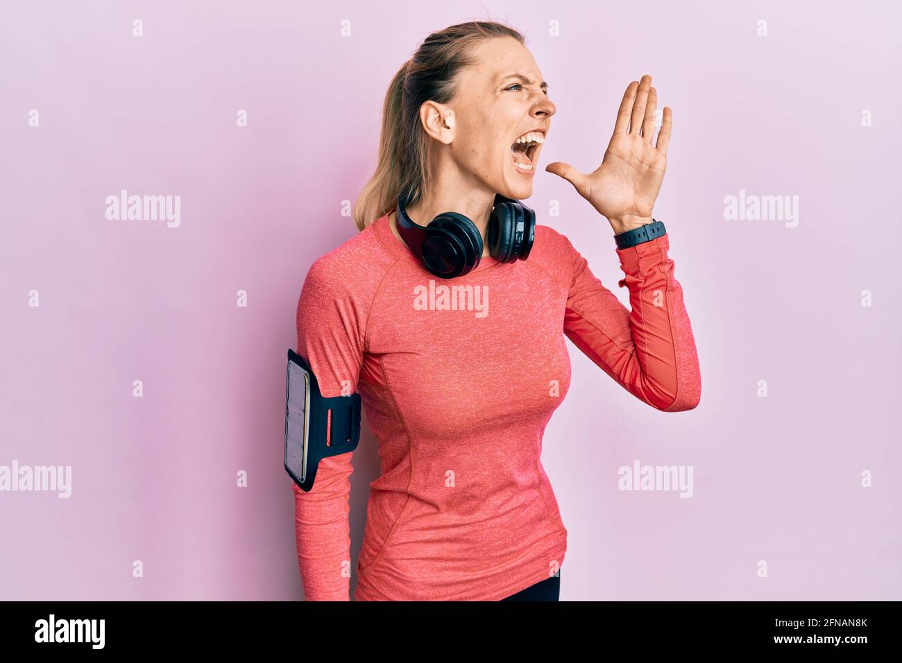 Beautiful caucasian woman wearing sportswear and arm band shouting and ...