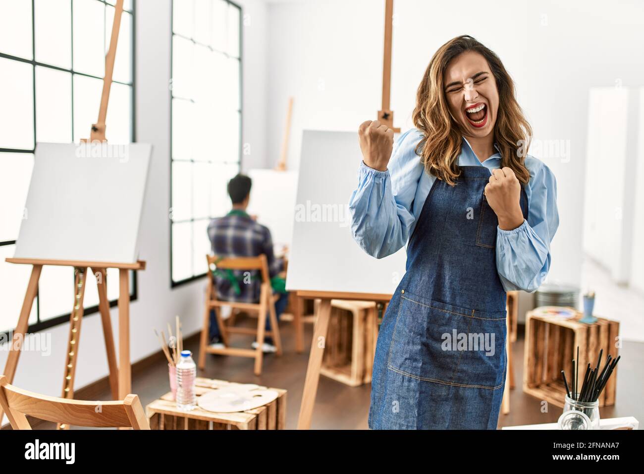 Young artist woman at art studio very happy and excited doing winner ...