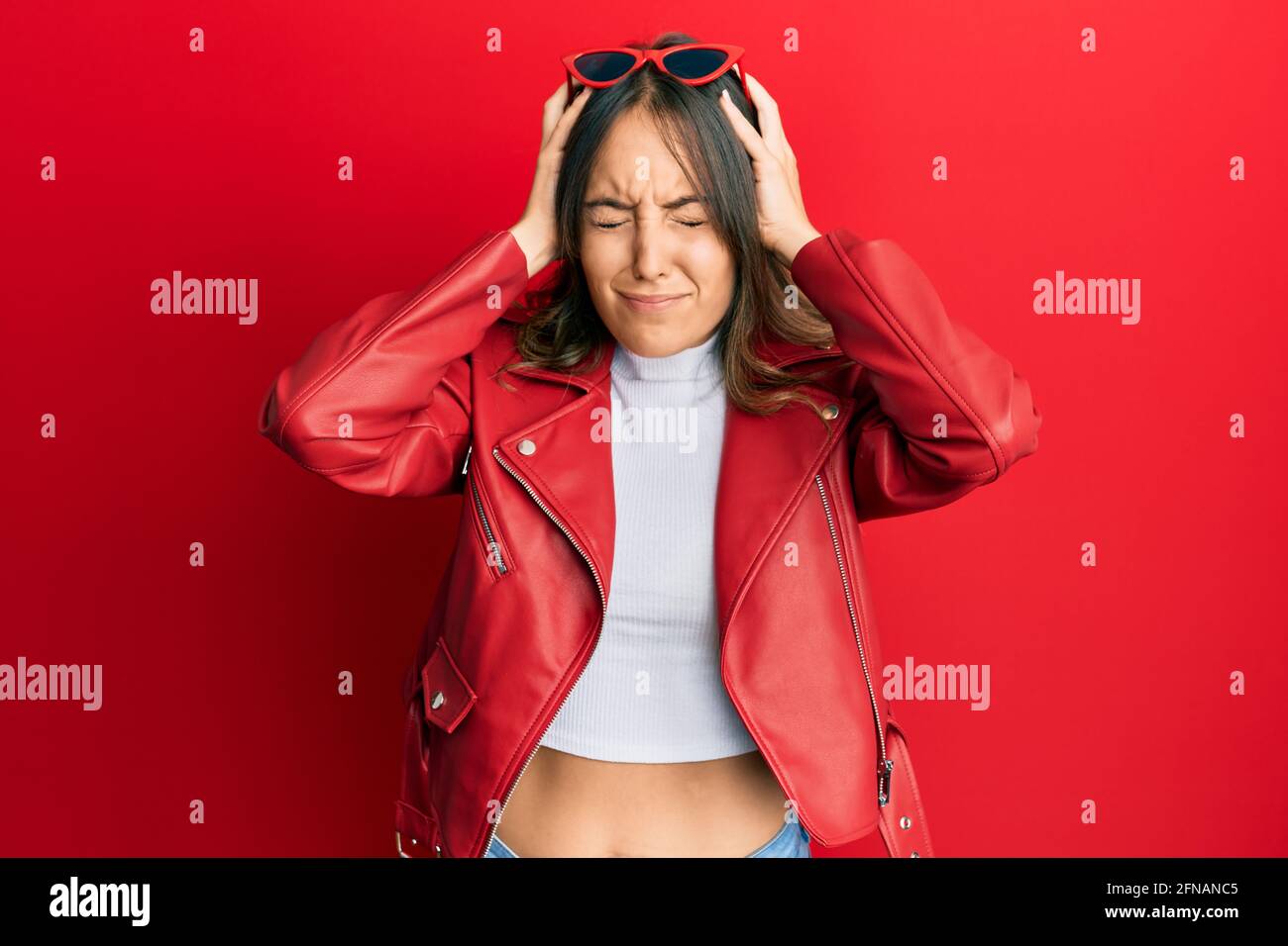 Young brunette woman wearing red leather jacket suffering from headache ...