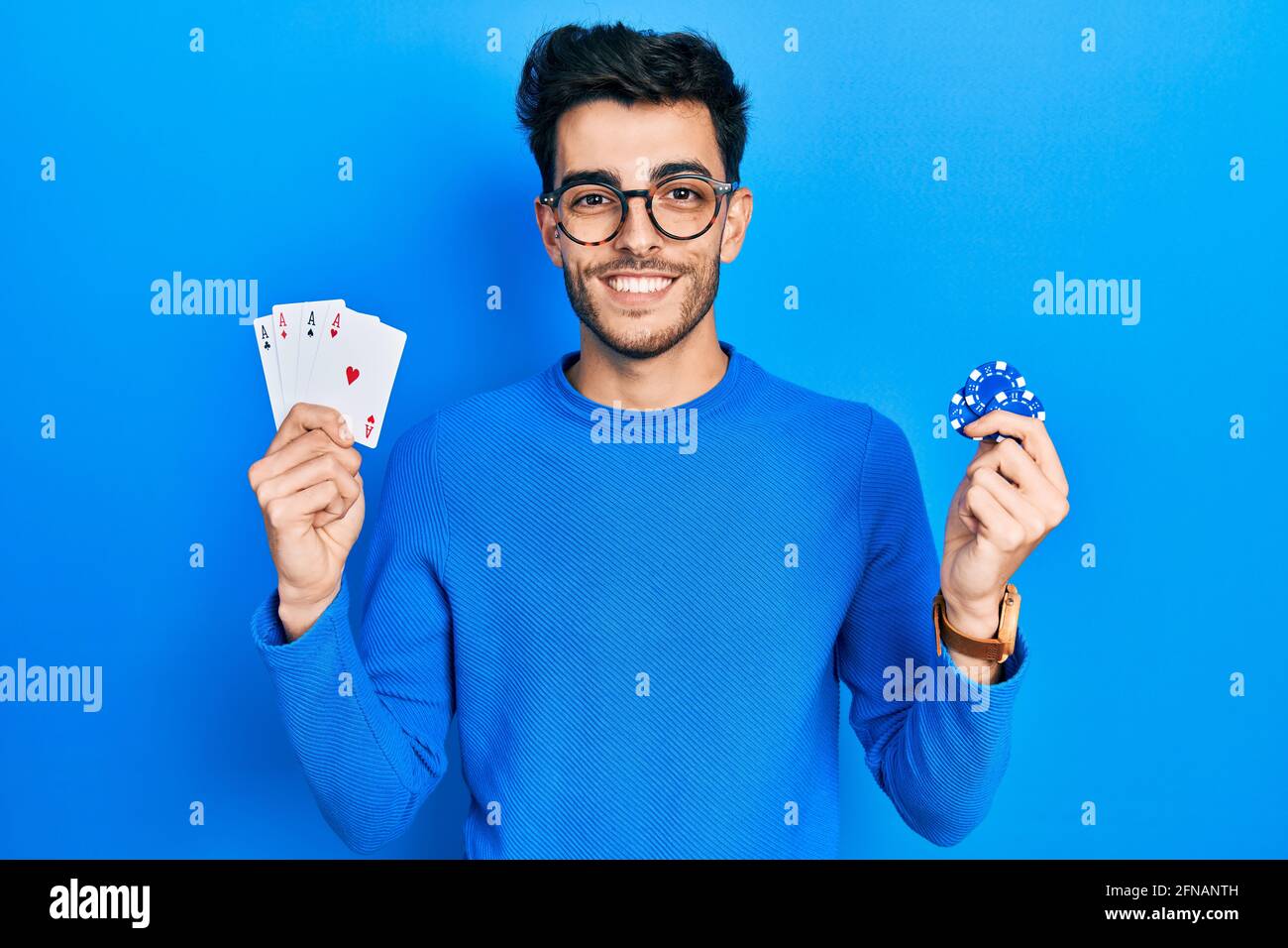 Young hispanic man playing poker holding casino chips and cards smiling ...