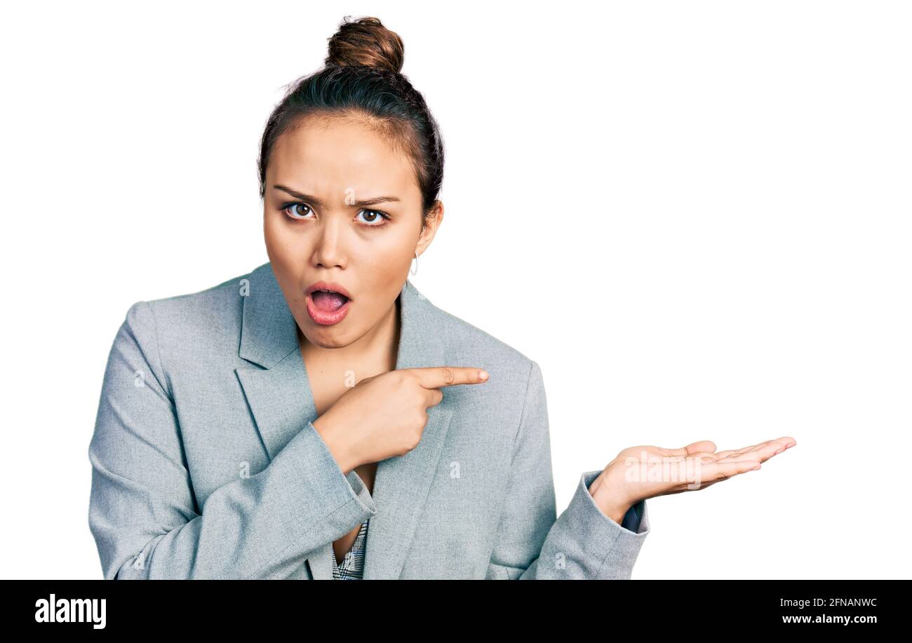 Young hispanic girl pointing open palm with finger in shock face ...