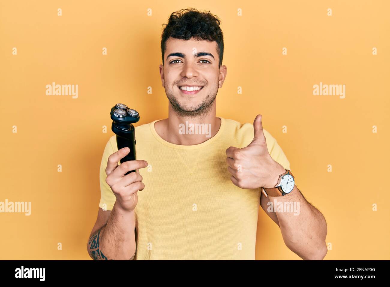 Young hispanic man holding electric razor smiling happy and positive ...