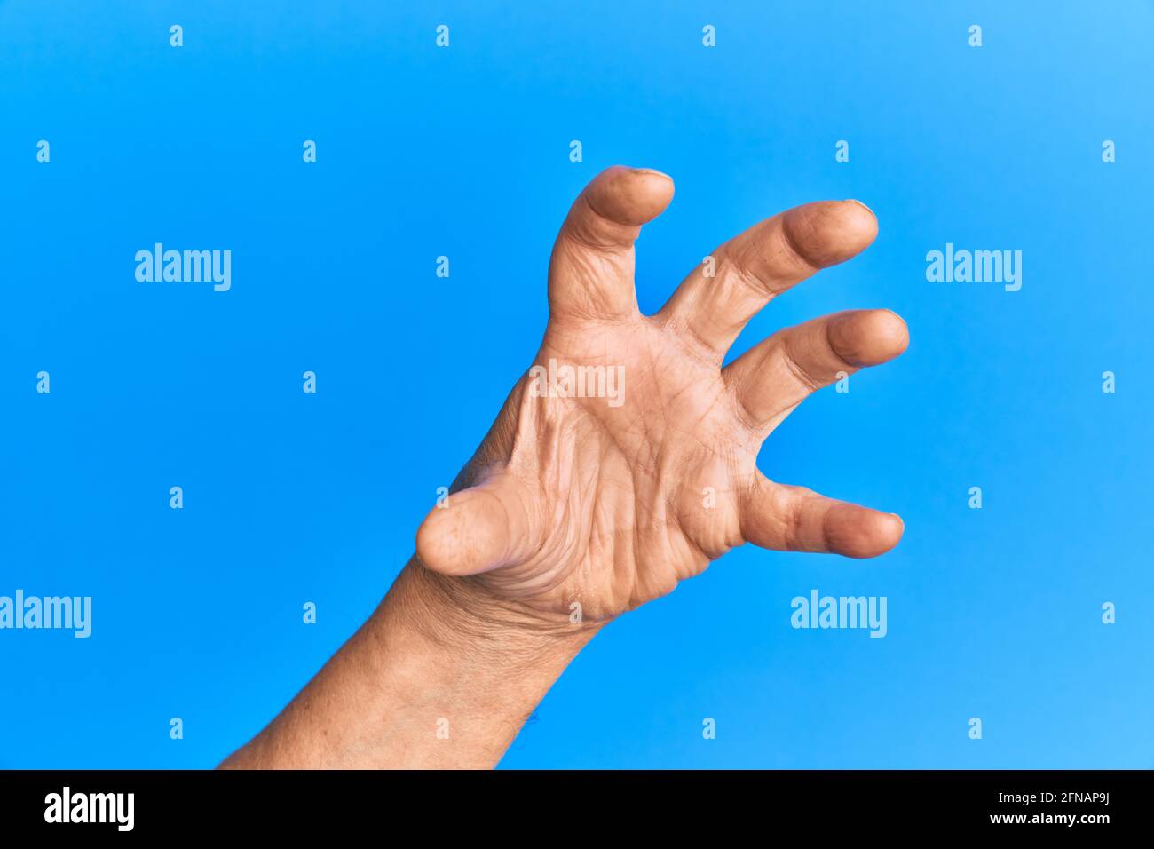 Hand of senior hispanic man over blue isolated background grasping ...