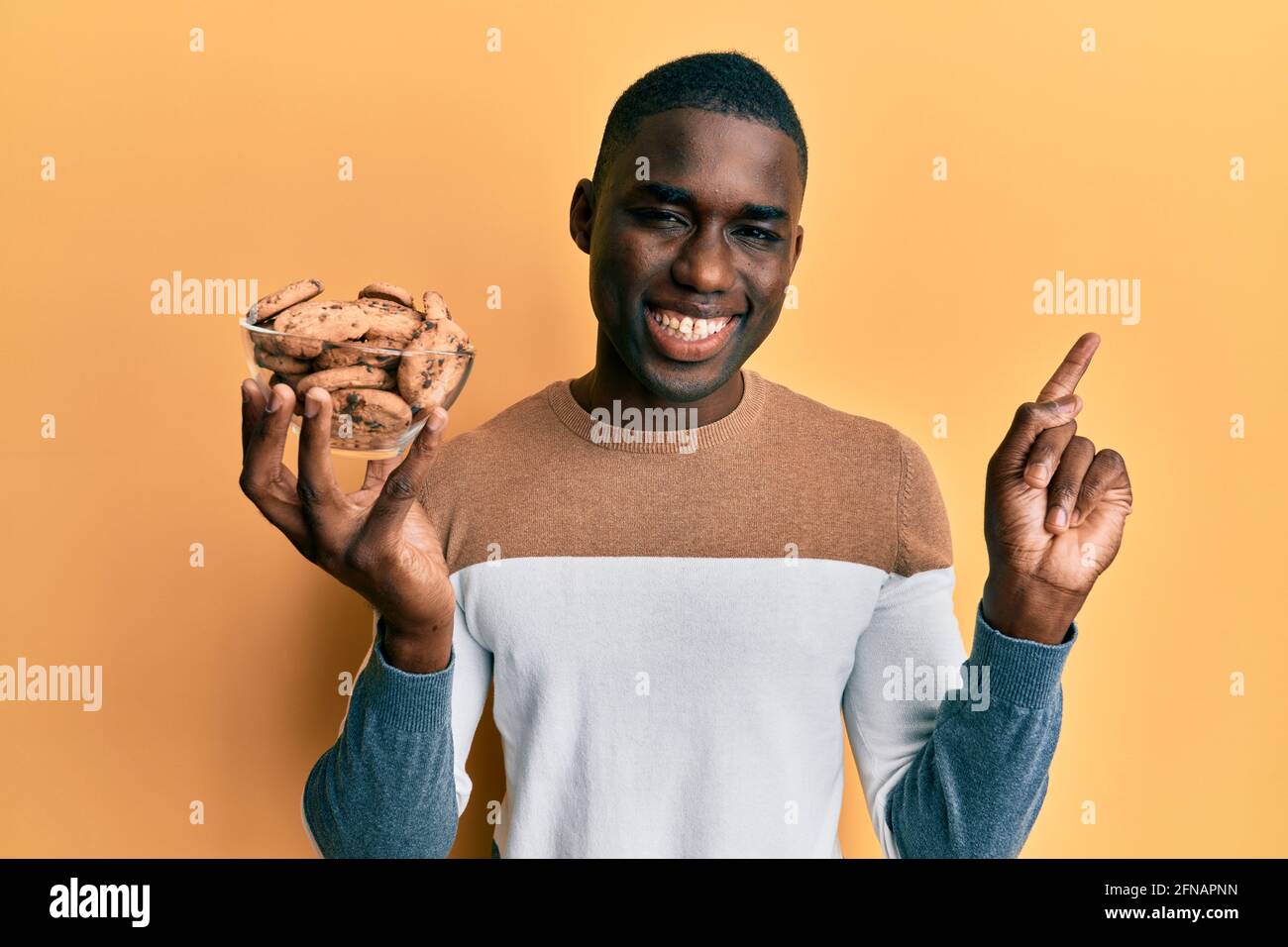 Young african american man holding bowl with chocolate chips cookies ...