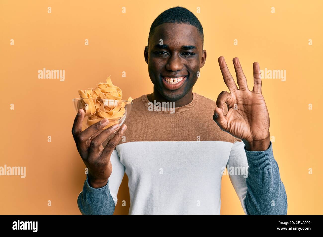 Young african american man holding bowl with uncooked spaghetti doing ...