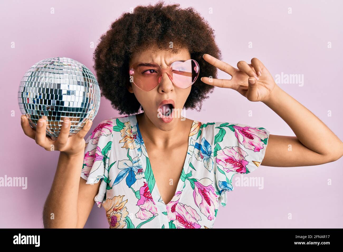 Young hispanic girl wearing summer style holding disco ball angry and ...