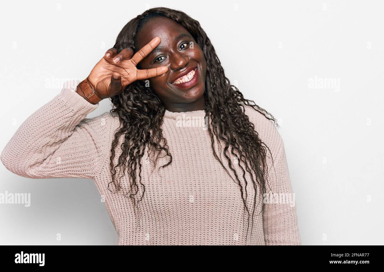 Young african woman wearing wool winter sweater doing peace symbol with ...