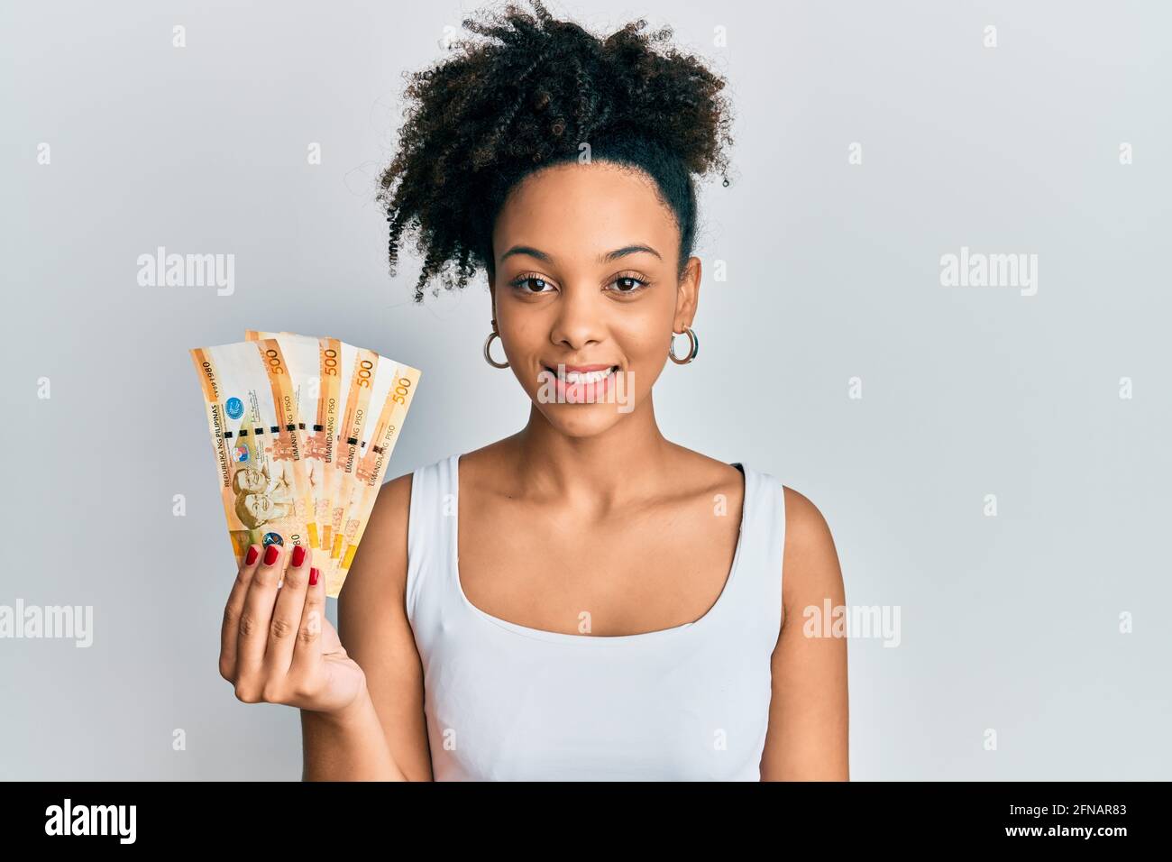 Young african american girl holding philippine peso banknotes looking ...