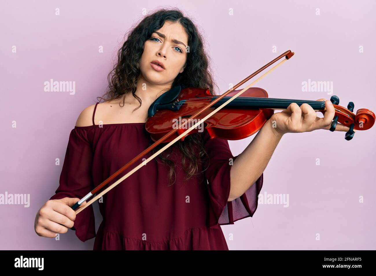 Young brunette musician woman with curly hair playing violin in shock ...