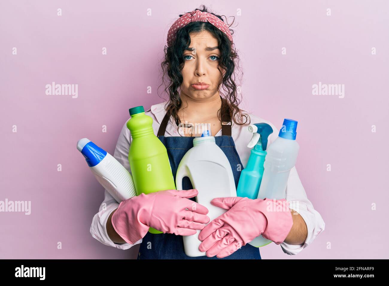 Young brunette woman with curly hair wearing cleaner apron holding ...