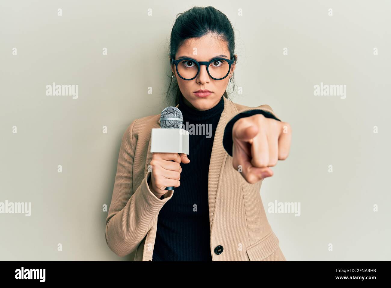 Young hispanic woman holding reporter microphone pointing with finger ...