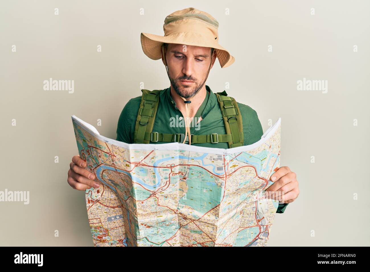 Handsome man with beard wearing explorer hat holding map relaxed with ...