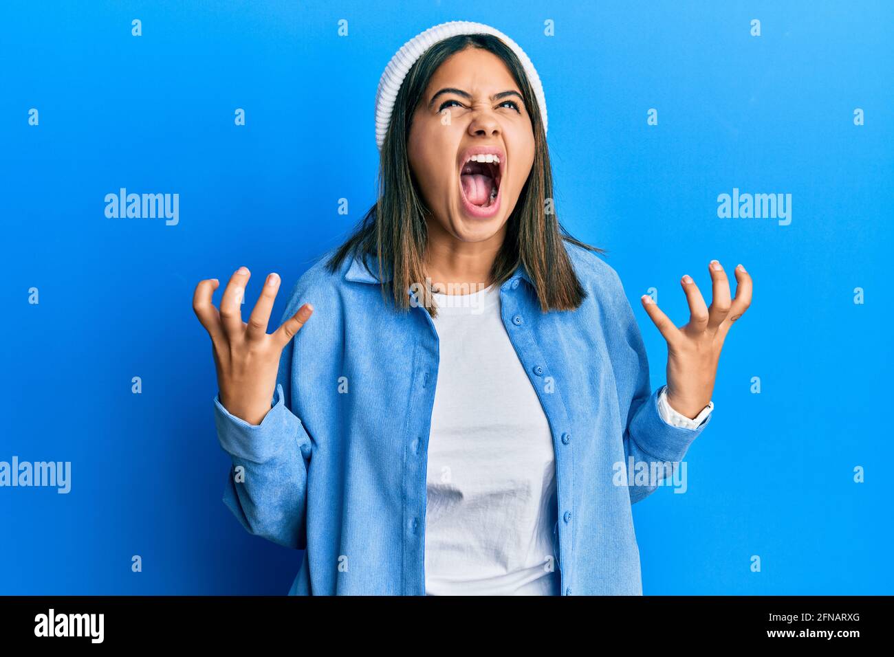 Young latin woman wearing cute wool cap crazy and mad shouting and ...