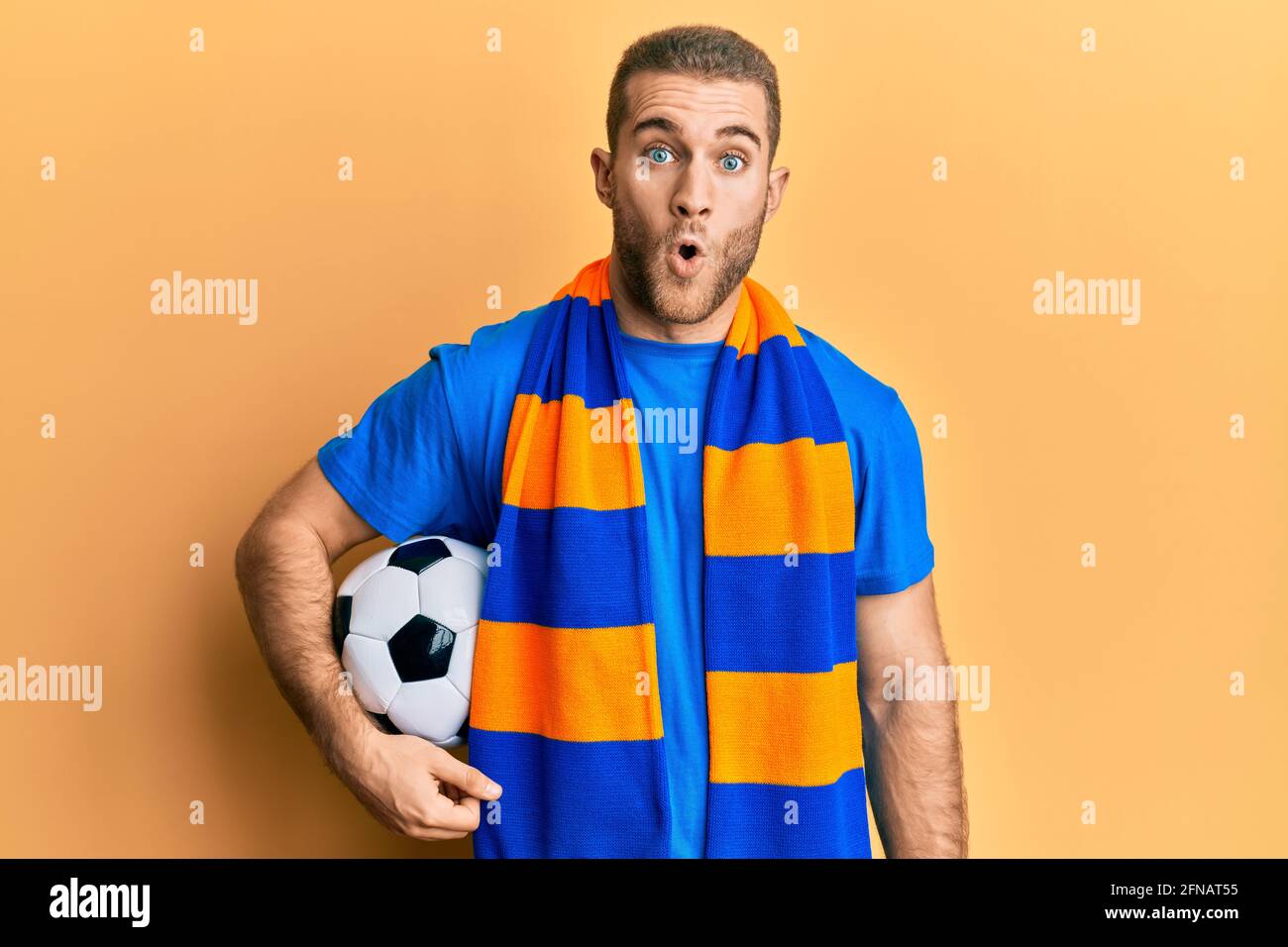 Young caucasian man football hooligan cheering game holding ball scared ...