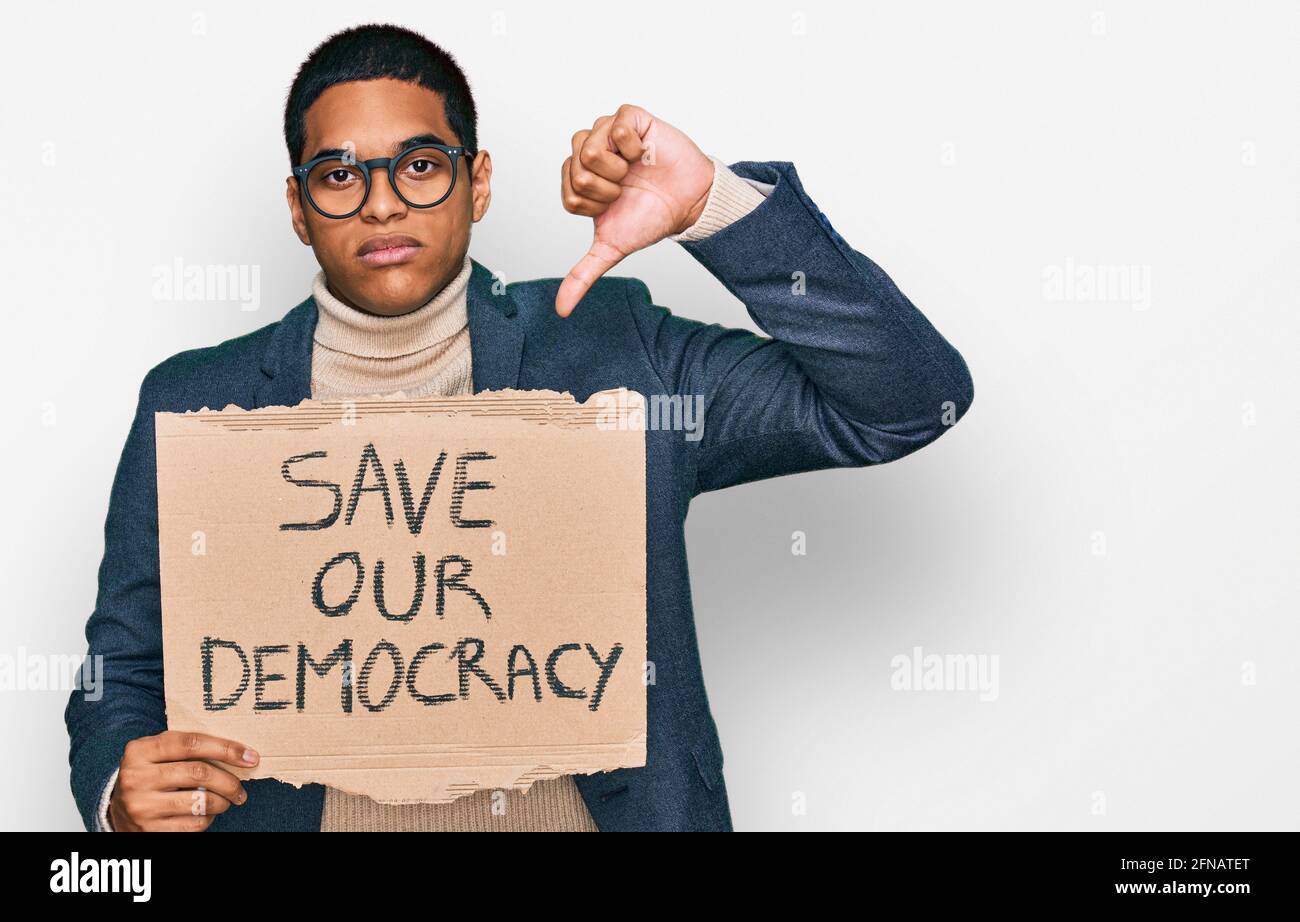 Young handsome hispanic man holding save our democracy protest banner ...