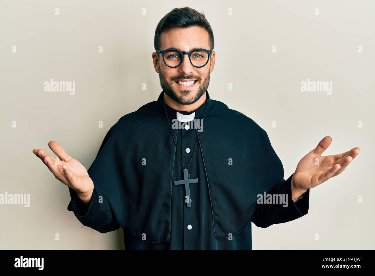 Young hispanic priest man standing over white background smiling with a ...