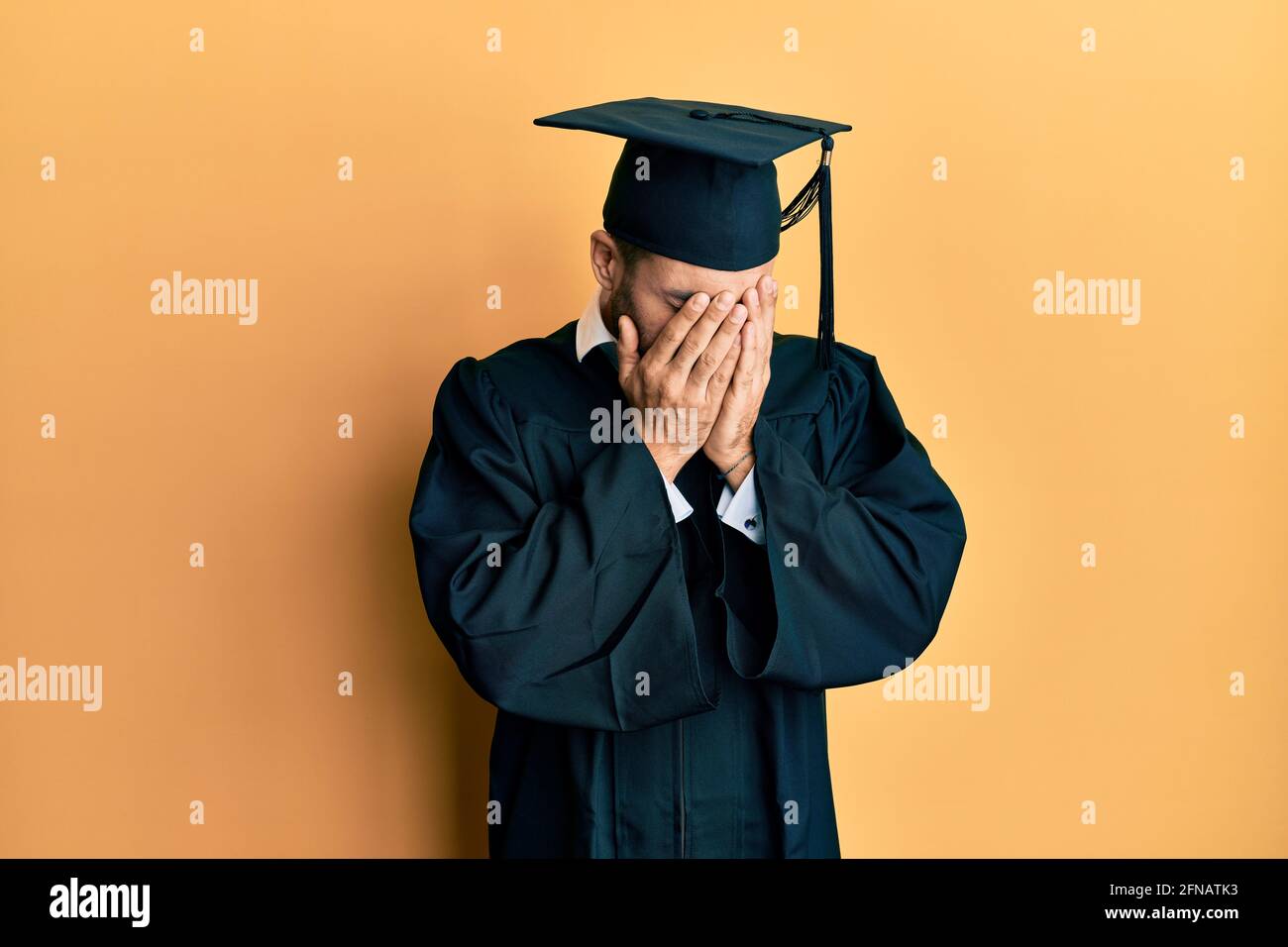 Young hispanic man wearing graduation cap and ceremony robe with sad ...