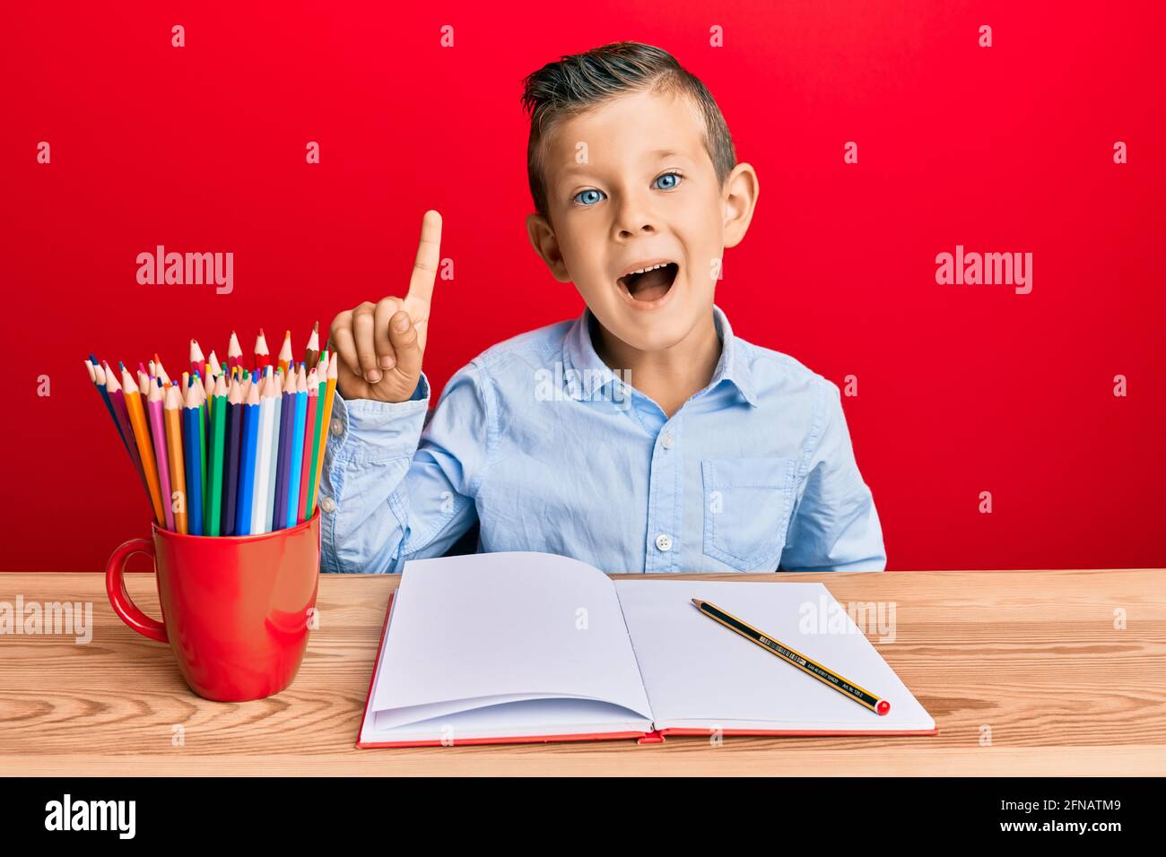 Adorable caucasian kid writing book sitting on the table smiling with ...