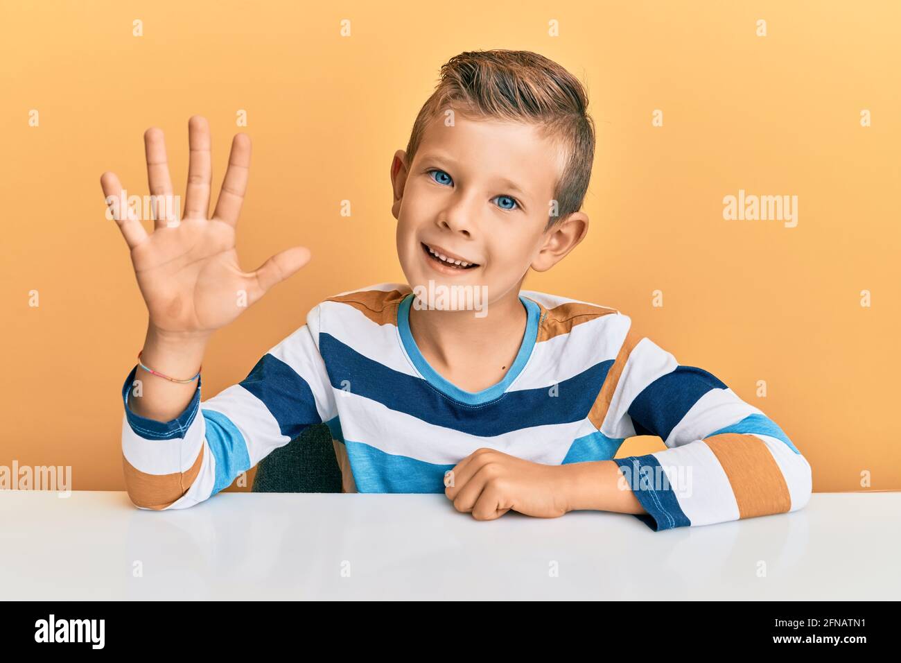 Adorable caucasian kid wearing casual clothes sitting on the table ...